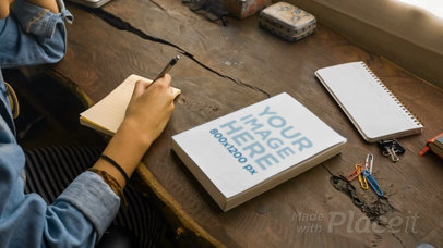 Placeit - Woman Writing in her Notepad With a Book Video Beside it