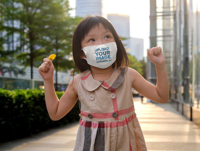 Placeit - Face Mask Mockup of a Happy Little Girl with a Candy in Her Hand